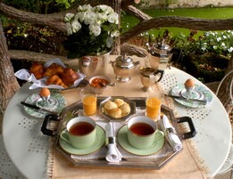 Uma mesa posta para o café da manhã, com chá, ovos, doces e suco.