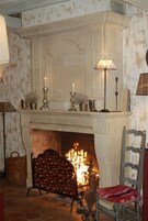 Uma lareira com fogo, uma arara com objetos decorativos e uma cadeira.