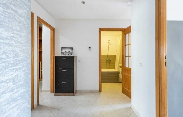 Um corredor com um guarda-roupa de madeira, um quadro na parede e uma escadaria que leva a um quarto com cortina amarela.