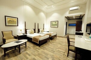 Quarto de hotel com duas camas, uma escrivaninha, uma cadeira e uma televisão.