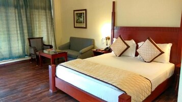 Quarto de hotel com uma cama grande, uma escrivaninha, uma cadeira e uma janela com cortinas.