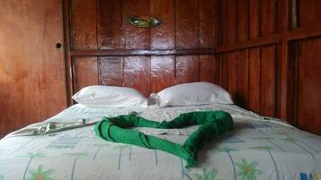 Uma cama com um cobre-leito estampado com flores, duas almofadas brancas e um objeto em formato de coração verde sobre a cama.