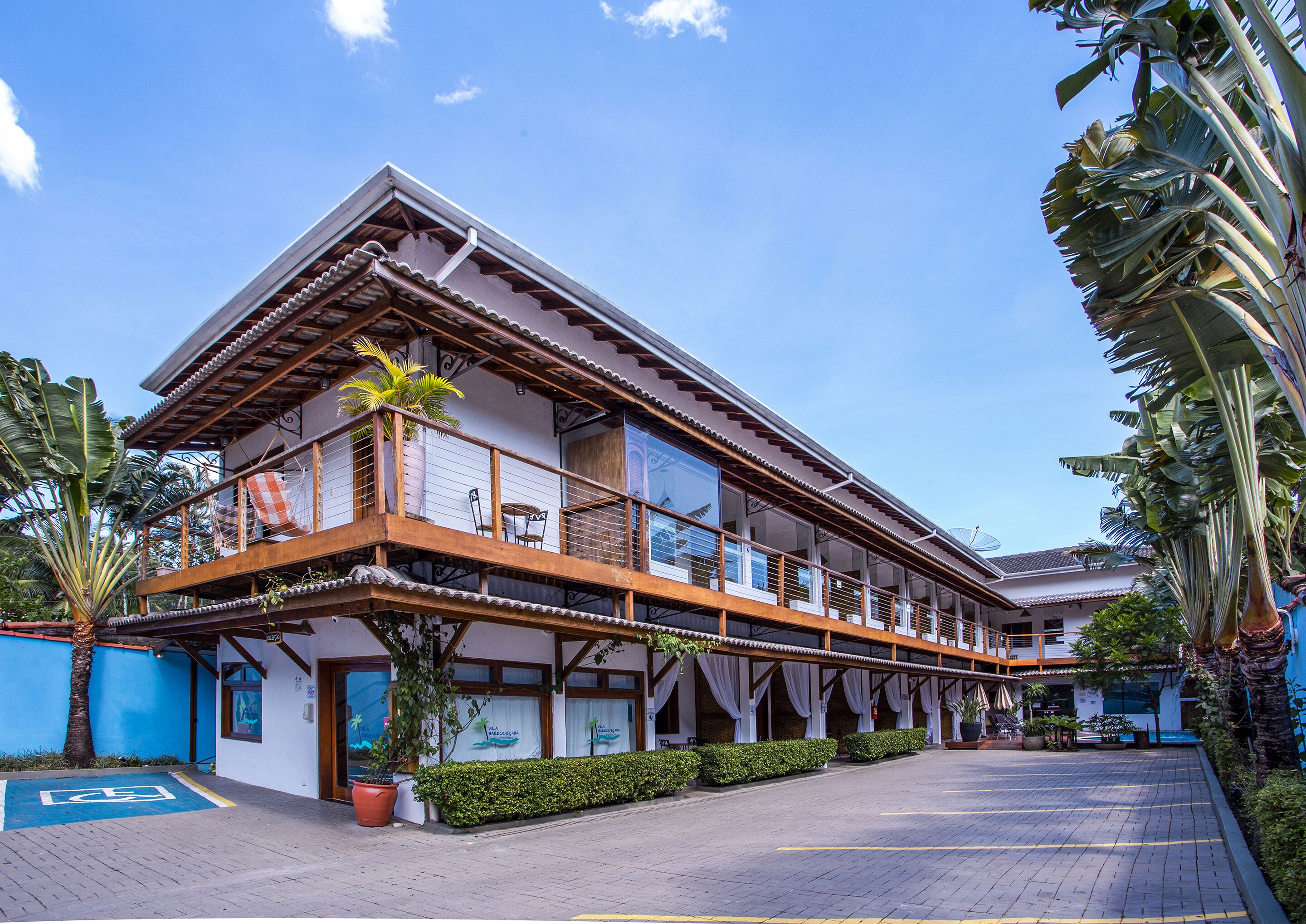 Um edifício de dois andares com varanda, plantas em vasos e vaga estacionamento acessível para cadeiras de rodas.