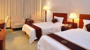 Quarto de hotel com duas camas, uma cadeira, uma escrivaninha e um abajur.