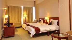 Quarto de hotel com duas camas, uma escrivaninha, uma cadeira e um abajur.