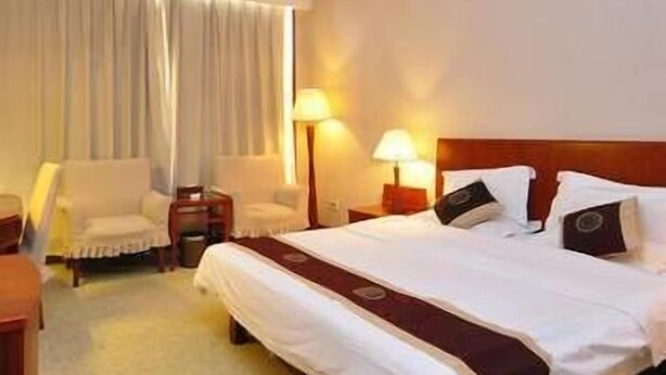 Quarto de hotel com uma cama grande, duas mesas de cabeceira, uma cadeira e um abajur.