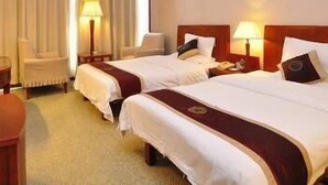 Quarto de hotel com duas camas, uma cadeira, uma escrivaninha e um abajur.