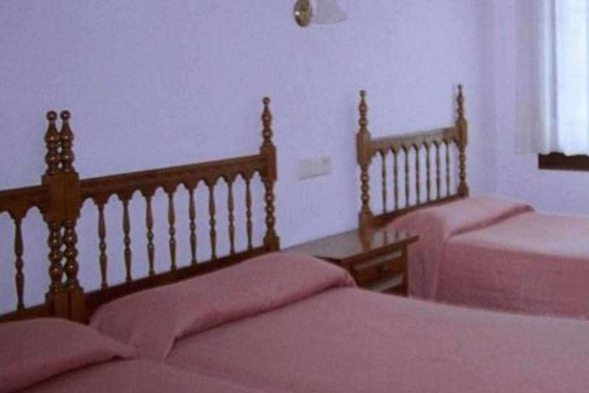 Quarto com duas camas de madeira com cabeceiras, uma janela com cortinas e um radiador.