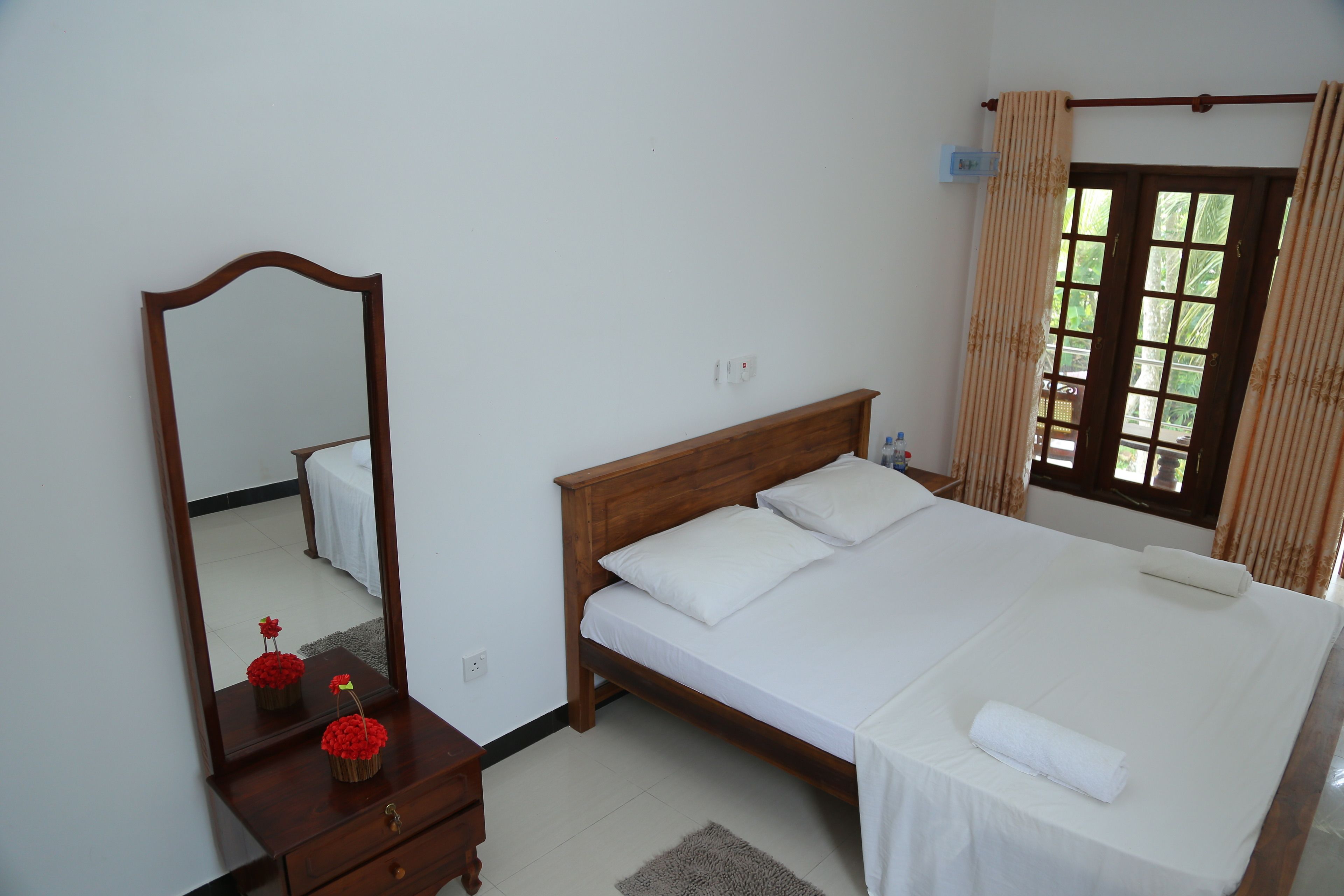 Quarto com cama de madeira, mesa de cabeceira, espelho e janela com cortinas.