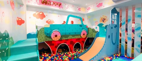 Espaço infantil com escorrega, piscina de bolinhas e decorações coloridas na parede.