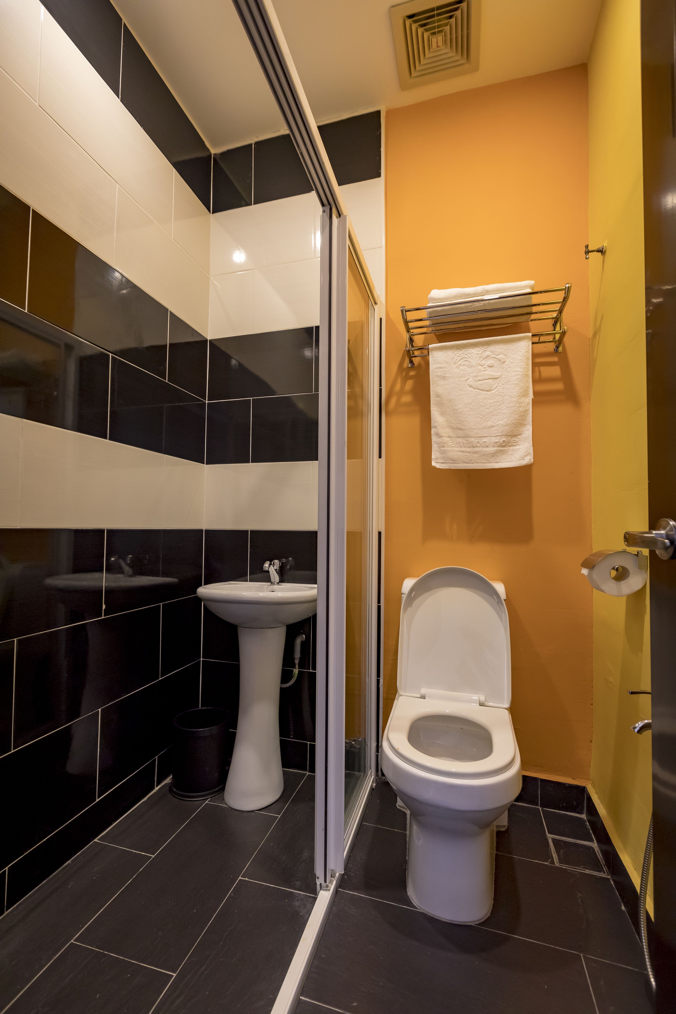 Casa de banho com paredes revestidas de azulejos preto e branco, uma sanita e lavatório brancos, e um porta-toalhas com uma toalha.