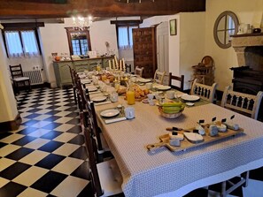Uma sala de jantar com piso quadriculado, uma mesa comprida posta para refeição e uma lareira.