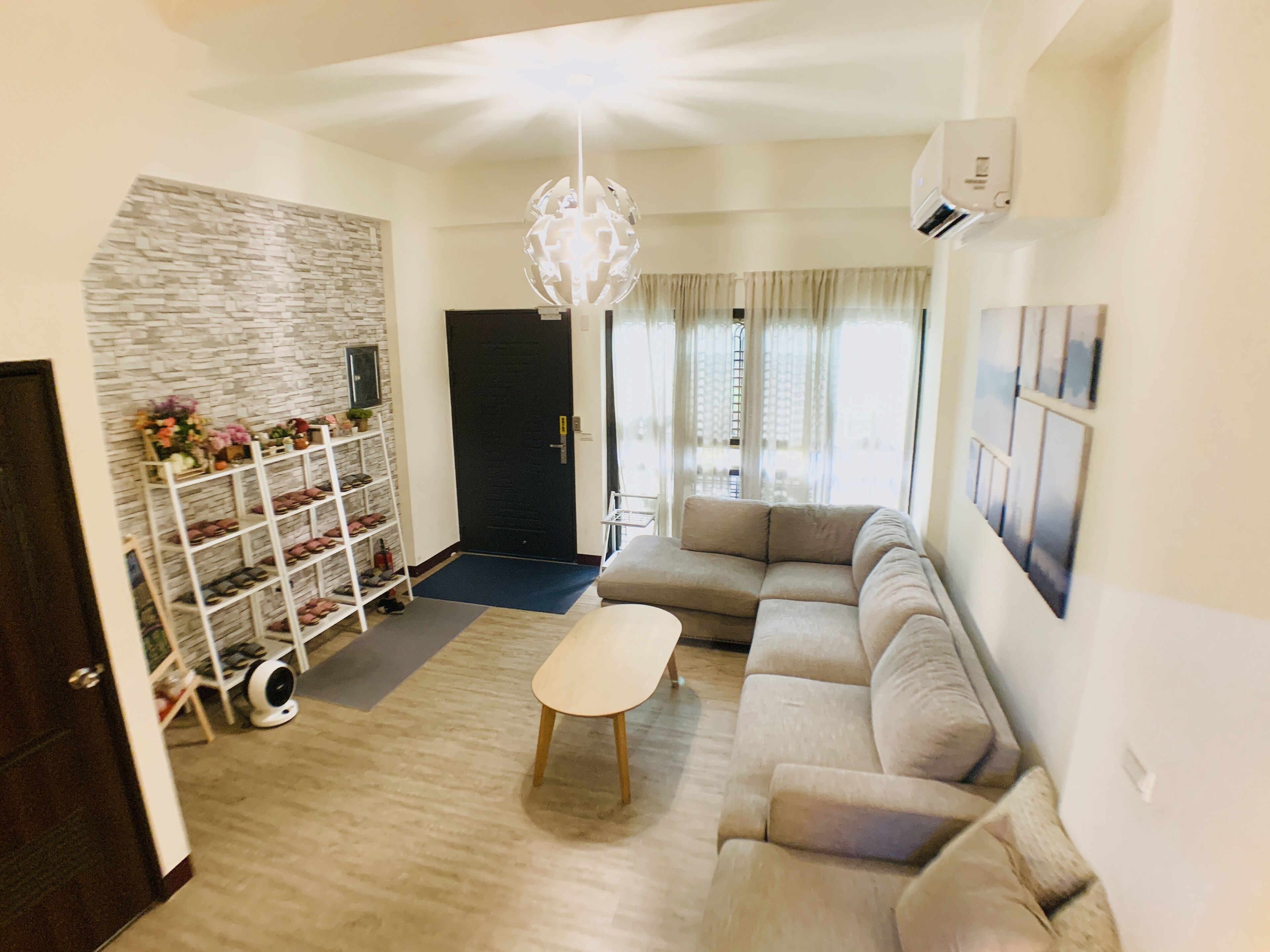 Sala de estar com sofá bege, mesa de centro branca, parede com textura de pedra, sapateira e lustre moderno.