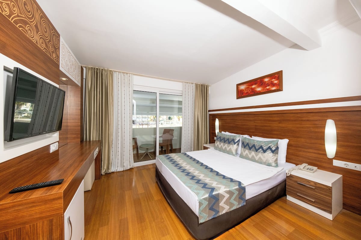 Quarto de hotel moderno com uma cama grande, televisão, mesa de cabeceira e vista para a cidade pela janela.