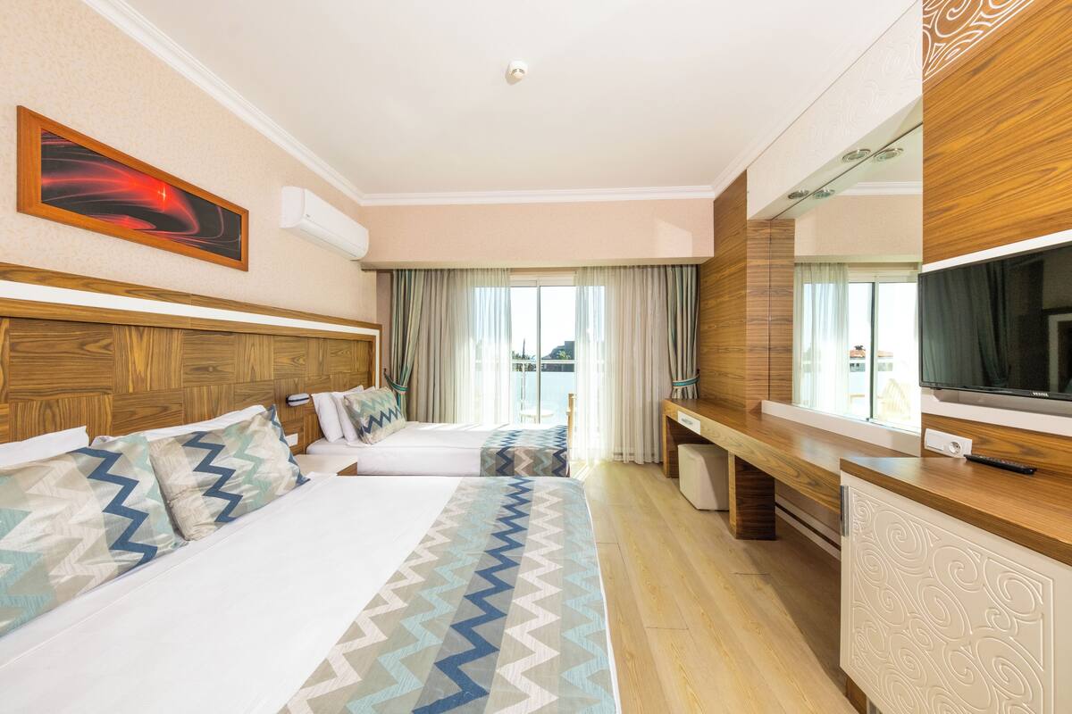 Quarto de hotel com duas camas, televisão, secretária e janela com cortinas.