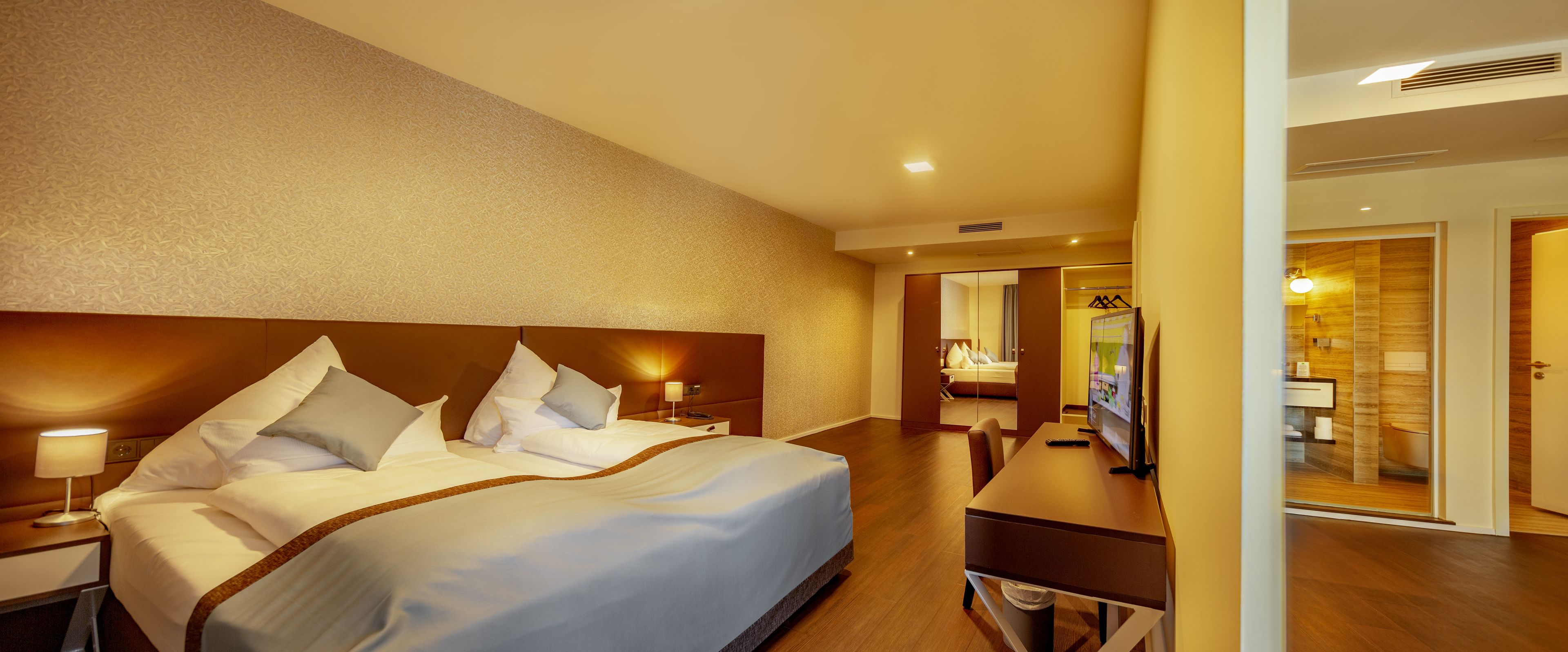 Quarto de hotel com cama grande, mesas de cabeceira, escrivaninha e espelho.