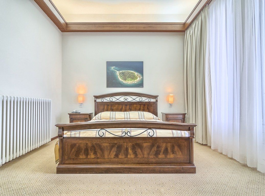 Quarto com cama de madeira, mesa de cabeceira, luminária na parede e quadro emoldurado.