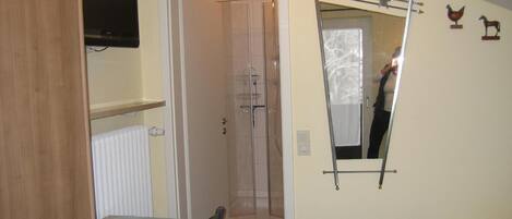 Quarto com cama, uma cadeira, televisão fixada na parede, espelho e porta para um banheiro.
