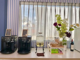 Um quarto com duas cafeteiras, um pote de vidro, um vaso com flores, uma vela e uma garrafa de vinho sobre uma mesa.