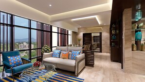 Uma sala de estar moderna com sofá, poltrona e mesa de centro, janelas amplas com vista para a cidade, e um aparador de vidro decorativo.