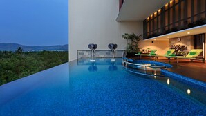 Uma piscina infinita com vista para as montanhas, espreguiçadeiras e um relógio na parede.