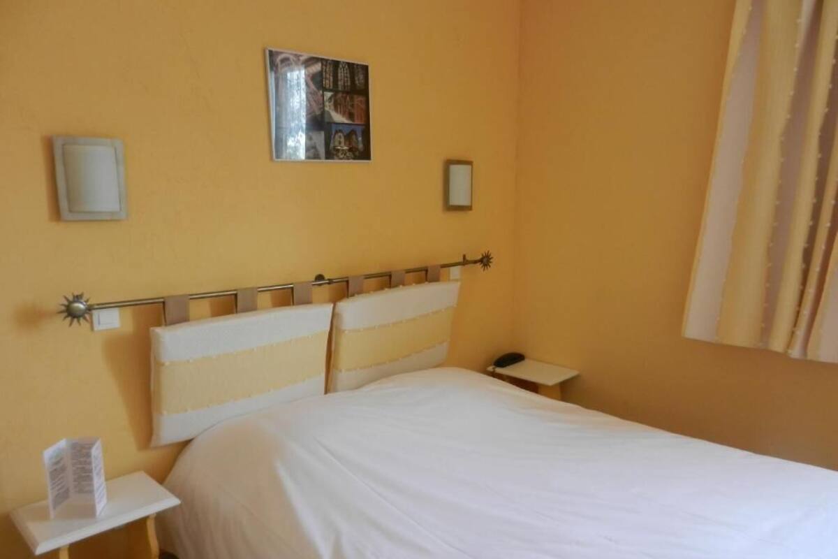 Quarto de hotel com cama, mesa de cabeceira e luminária na parede.