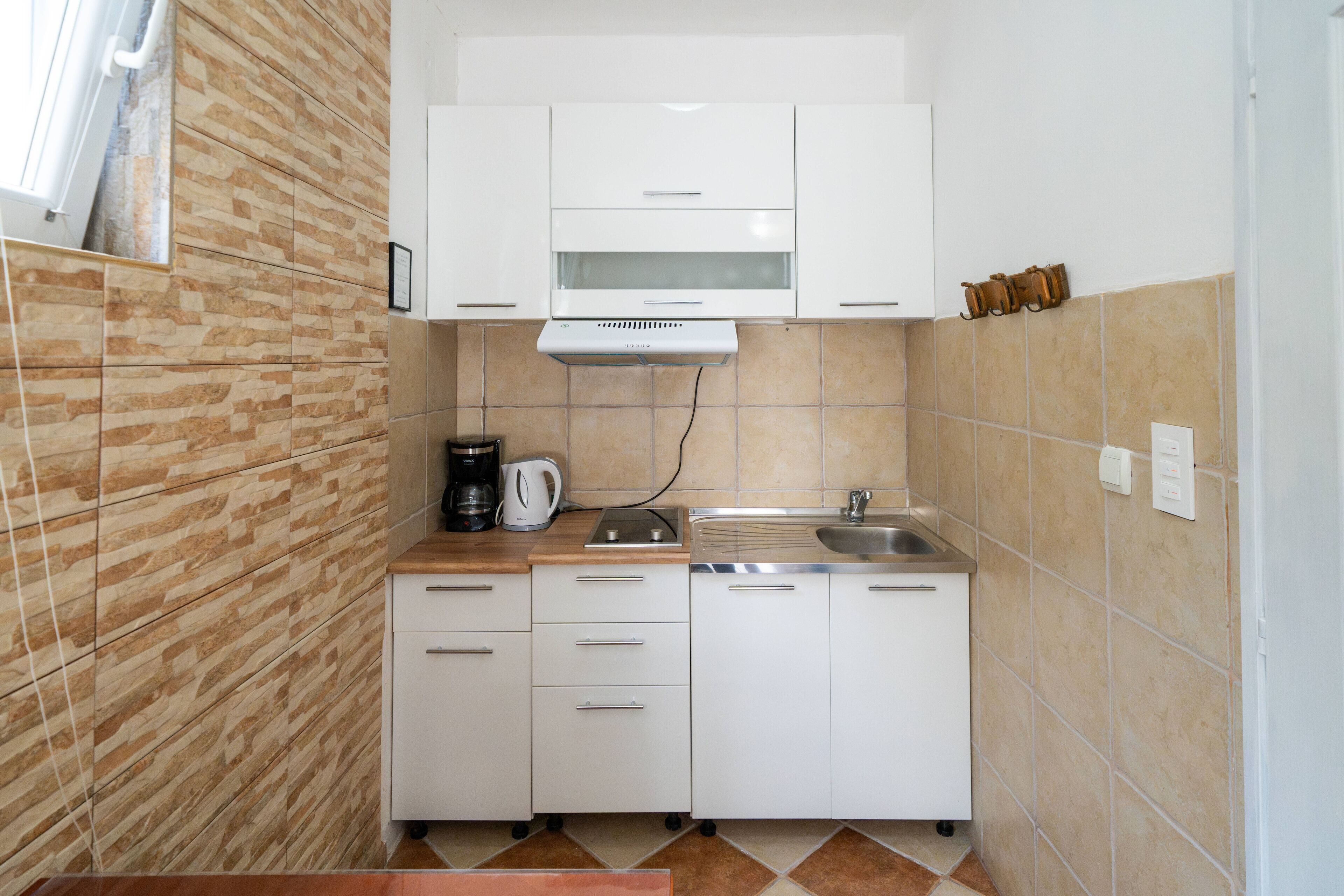 Cozinha compacta com armários brancos, pia de aço inoxidável e coifa embutida.