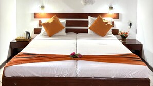 Uma cama de casal com cabeceira de madeira, roupa de cama branca, dois travesseiros laranja, um objeto decorativo e um mosquiteiro acima.