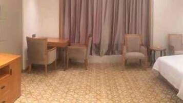 Quarto de hotel com cama, escrivaninha, duas cadeiras, uma mesinha e chão estampado.