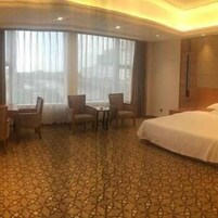 Quarto de hotel com uma cama grande, uma escrivaninha com cadeiras e vista para a cidade através de grandes janelas.