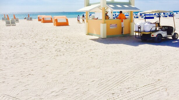 Uma praia com um posto de salva-vidas, cadeiras de praia e um carrinho de golfe.