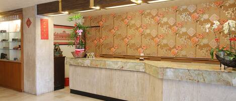 Uma área de recepção com balcão de mármore, papel de parede floral e exposição de artesanato local.