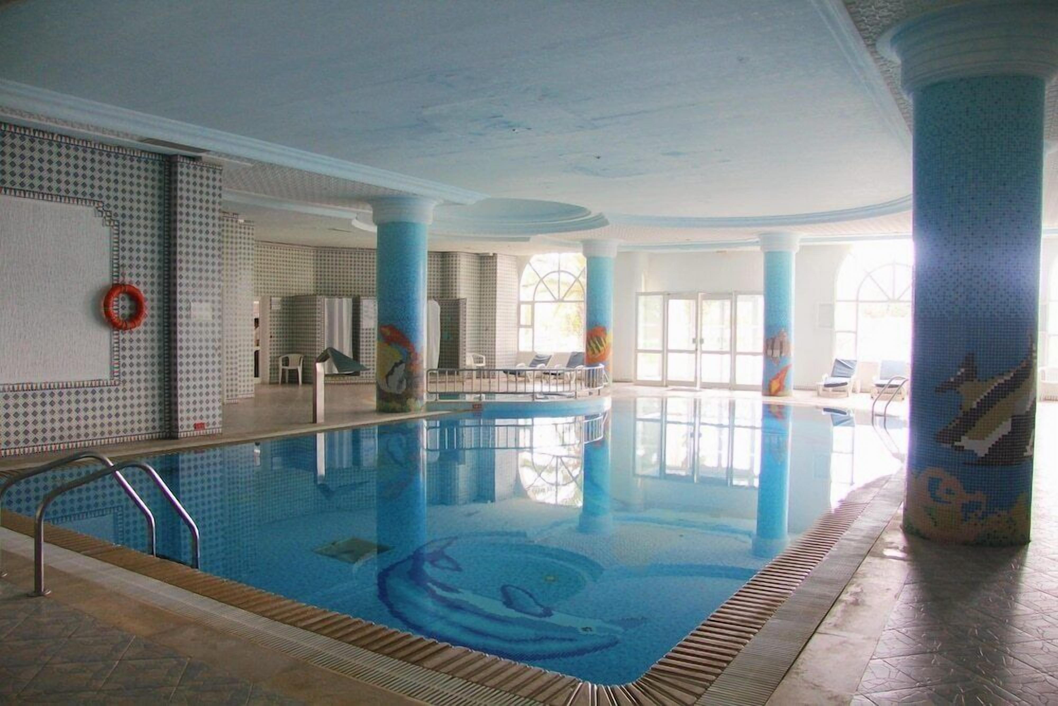 Piscina interior com água cristalina, paredes azulejadas e um boi salva-vidas à esquerda.