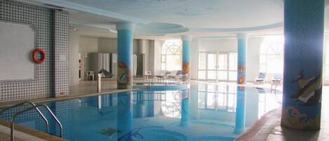 Piscina interior com água cristalina, paredes azulejadas e um boi salva-vidas à esquerda.