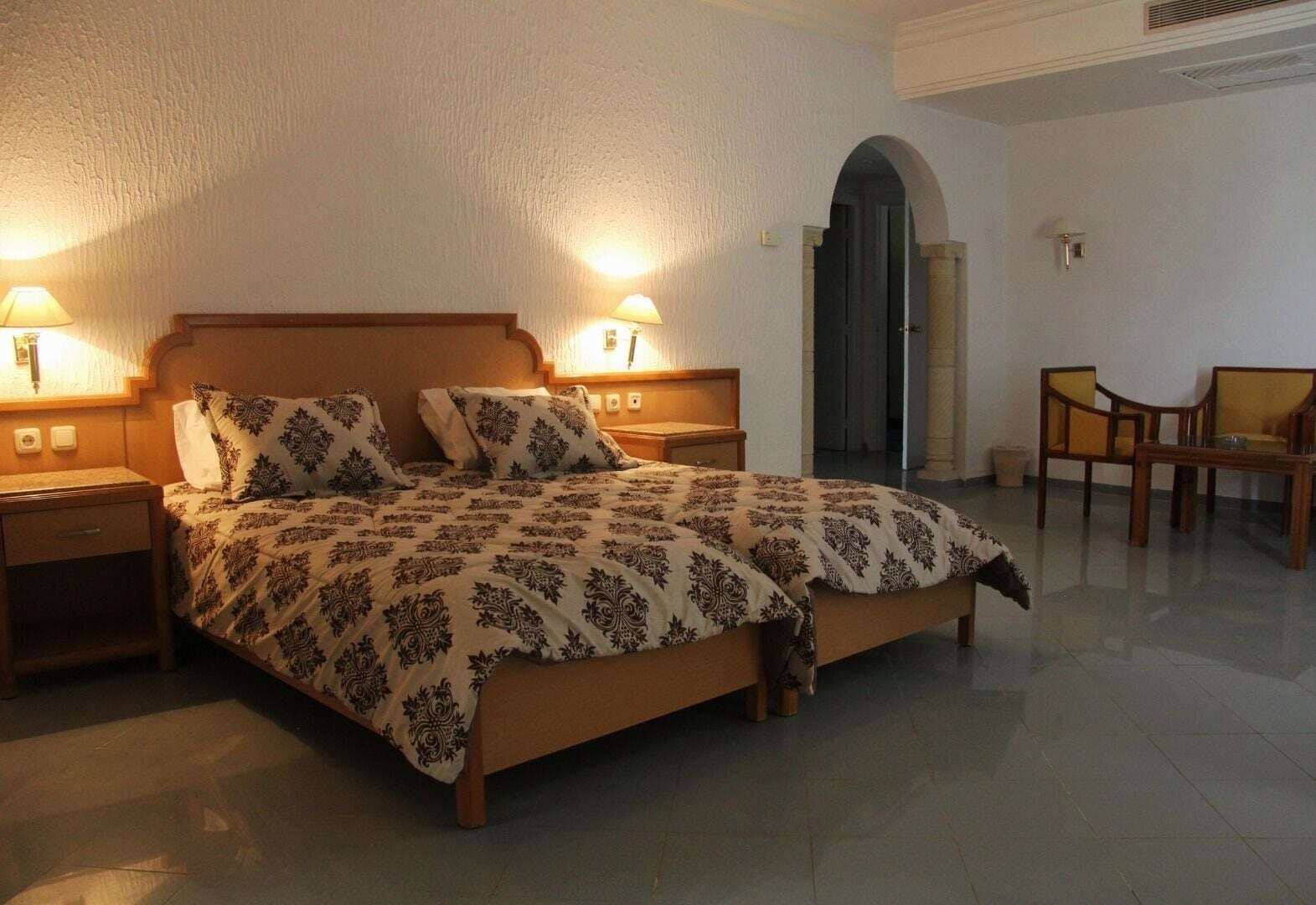 Um quarto com uma cama, duas luminárias de cabeceira, uma cadeira e uma porta.
