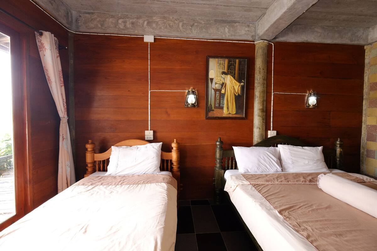 Quarto de hotel com duas camas, cabeceiras de madeira, um quadro na parede e duas luminárias.