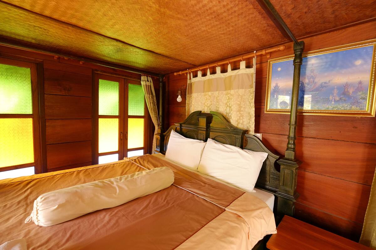 Um quarto de madeira com uma cama, uma janela com cortinas e um quadro na parede.