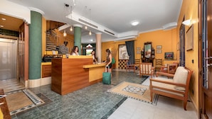 Um hall de hotel com balcão de atendimento, escada, sofá e tapete estampado.