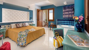 Um quarto espaçoso com uma cama grande, uma escrivaninha com um vaso de flores e vista para o exterior.