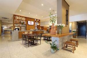 Um lobby de hotel moderno com área de bar, espaços de estar e balcão de recepção.