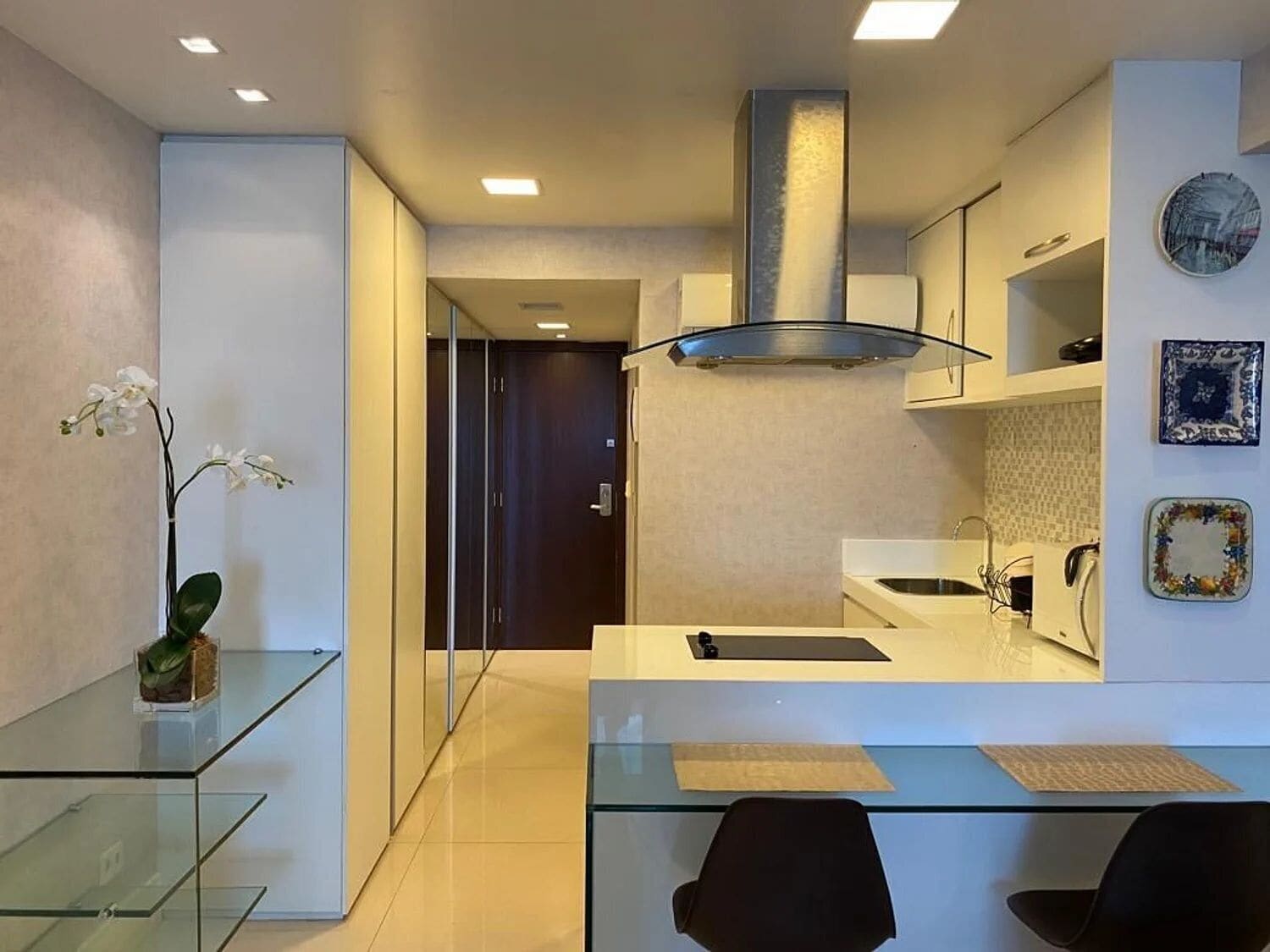 Cozinha moderna com mesa de jantar de vidro, uma cadeira preta e uma orquídea ornamental.