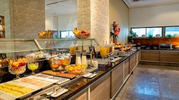 Buffet variado com diversas opções de alimentos e bebidas, incluindo frutas, doces e sucos.