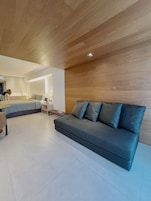 Quarto de hotel moderno com uma cama grande, um sofá, uma mesinha e uma área de cozinha planejada.