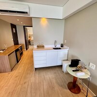 Cozinha compacta com bancada branca, pia e pequena mesa com telefone e copos.