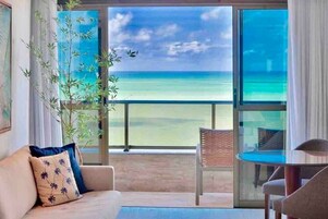 Quarto com vista para o oceano, um sofá com almofada decorativa, uma cadeira e uma mesa de vidro.
