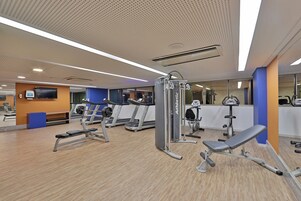 Academia com esteiras, máquinas de musculação e bancos.