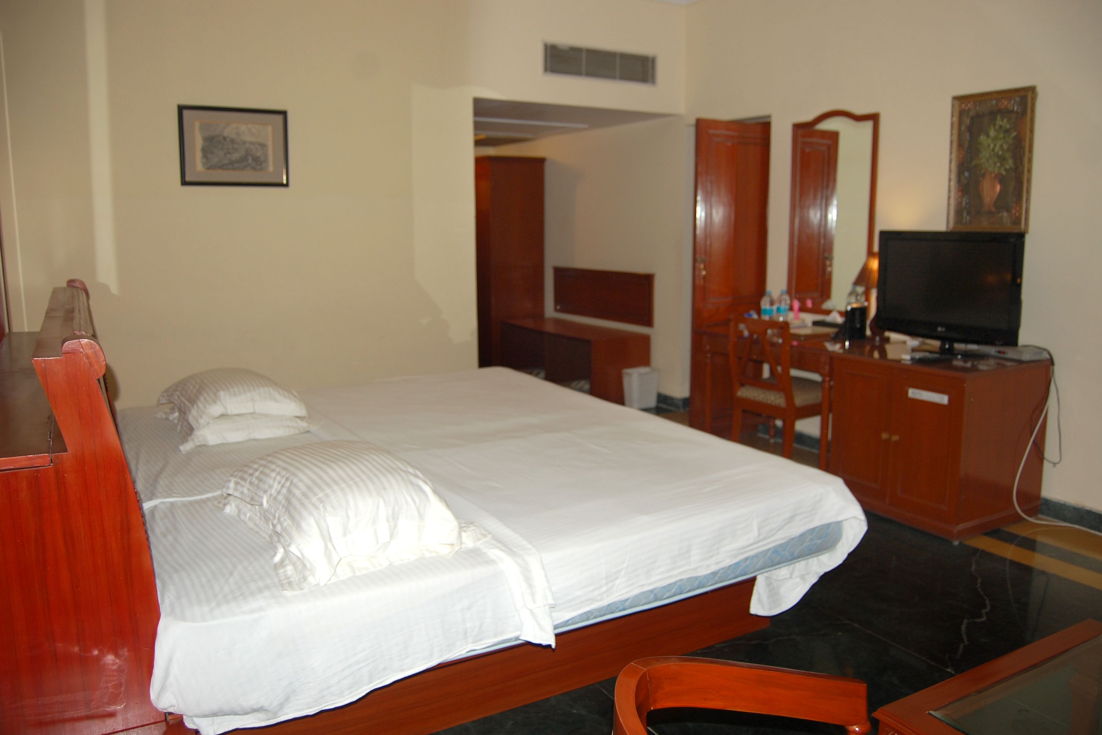 Quarto de hotel com uma cama, escrivaninha, cadeira, televisão e guarda-roupa.