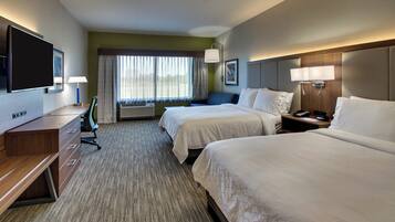 Quarto de hotel com duas camas, uma escrivaninha, uma cadeira, televisão e janela com cortinas.
