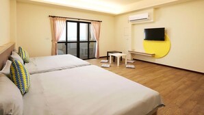 Quarto de hotel com duas camas, uma mesinha, uma cadeira, janela com cortinas, ar condicionado e uma televisão fixada na parede.