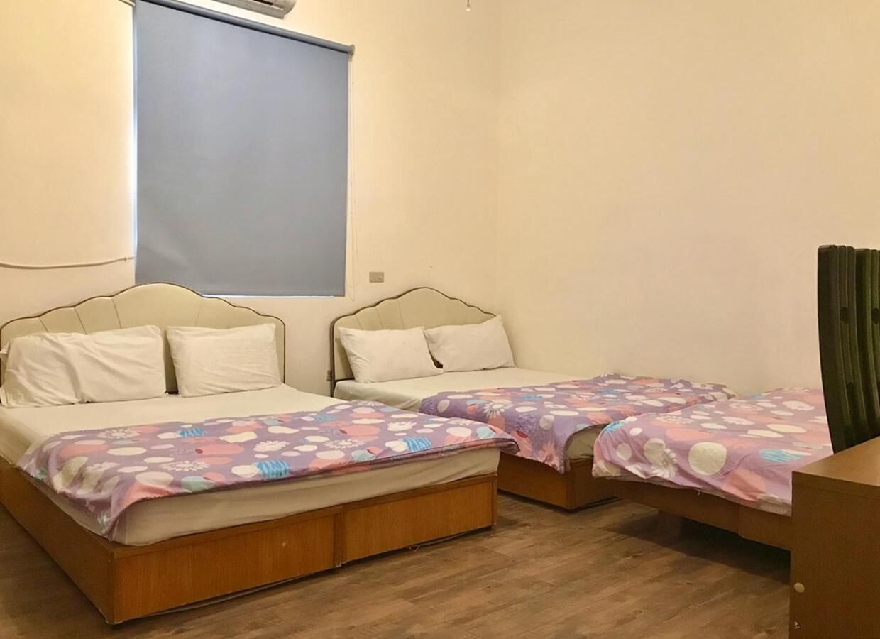Quarto com duas camas, cada uma com estrutura de madeira e edredom colorido. Há uma pequena escrivaninha à direita.